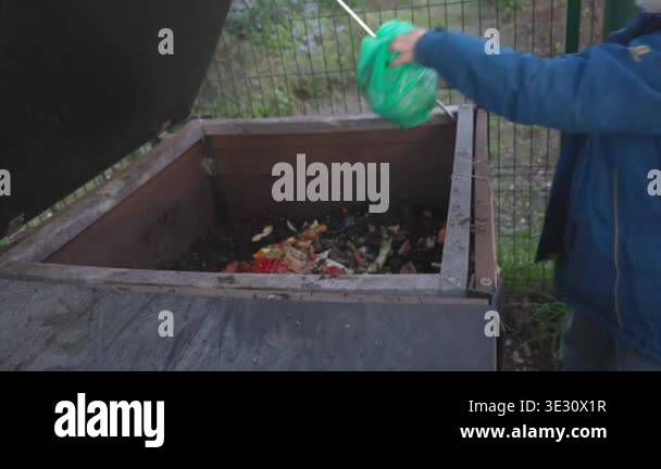 Person responsibly discards kitchen scraps into a wooden compost bin ...