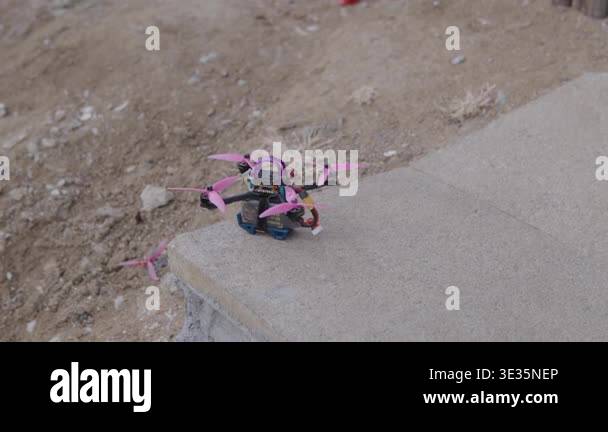 Small racing drone perched on a concrete ledge overlooking a dirt ...