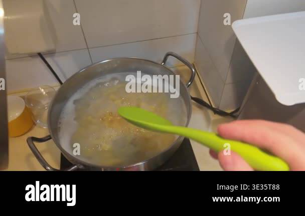 Hands stirring pasta in a pot of boiling water on a stovetop, steam ...