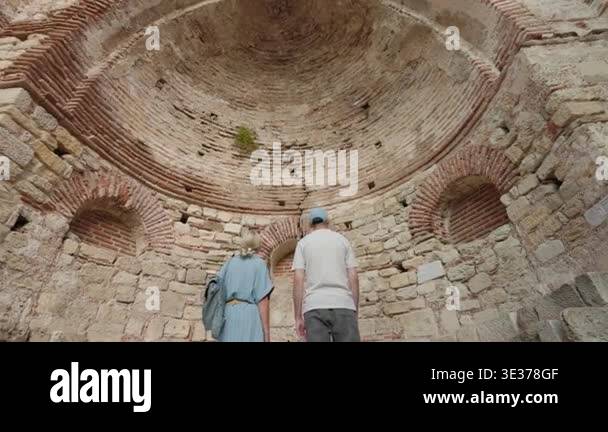 Tourists looking up at ancient church dome ruins with brick and stone ...