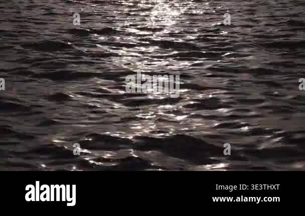 Bright sunlight creates a glowing path across dark ocean waves ...