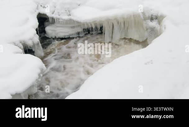 Partially frozen rapid with thick ice formations and icicles hanging ...