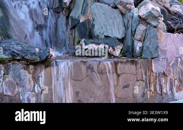 Small streams of water spill over stone ledges of a decorative rock ...