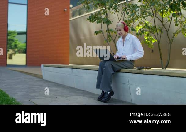 A young woman in red headphones scrolls on a laptop while sitting ...