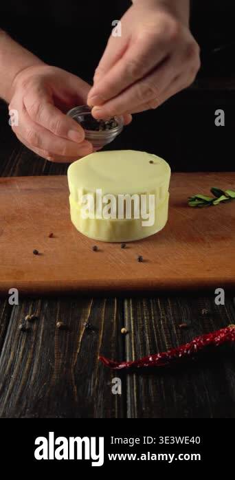 Hands carefully sprinkle peppercorns onto a round block of cheese ...