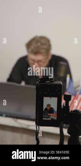 A vertical static shot through a camera lens showing a man sitting at a ...