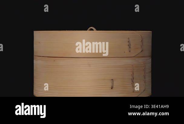 Against a dark backdrop, a hand lifts the lid of a traditional bamboo ...