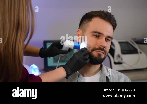 Female dermatologist examining a male patients skin with a special tool ...