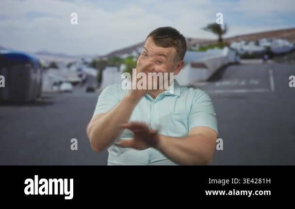 Man in a light blue shirt raising hands to block and wave palms forward ...