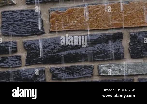 Raindrops fall vertically onto a brick wall. Bricks show black, brown ...
