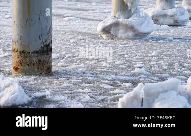 Textured icy sea slush and snow clusters envelop rusted metal pillars ...