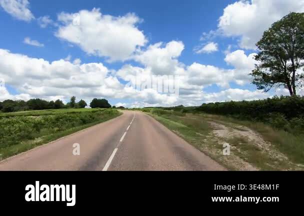 Empty country road stretching through lush green fields and trees in ...