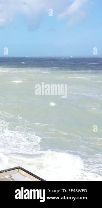 Rough ocean waves crash against a concrete seawall under a partly ...