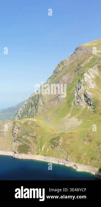 Steep rocky mountain slope rising above a clear blue alpine lake under ...