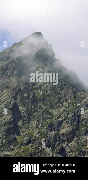 Dramatic rocky mountain peak shrouded in mist and low clouds in the ...