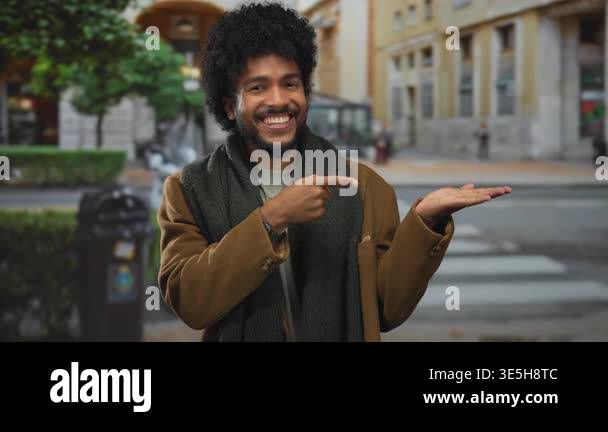 Happy man smiling outdoors on city street while pointing to his hand in ...