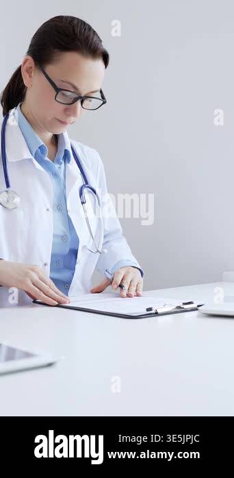 Middle aged female doctor completing healthcare paperwork, clipboard ...
