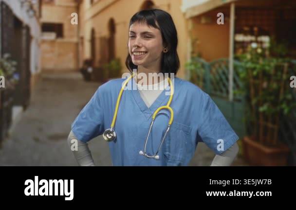 Woman in blue scrubs with stethoscope stands with hands on hips on ...