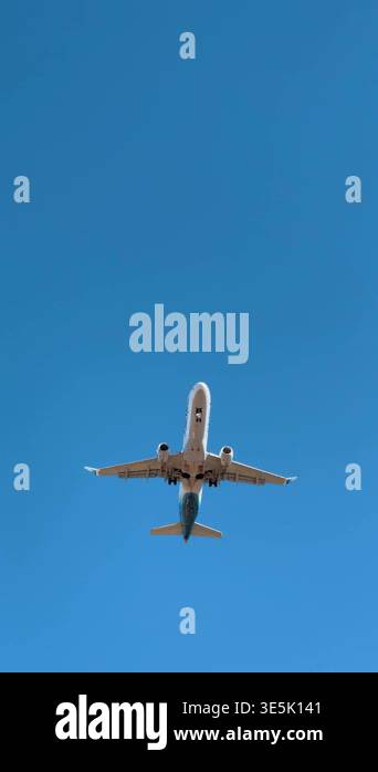 Bottom view of jet airplane landing against blue sky. Directly ...
