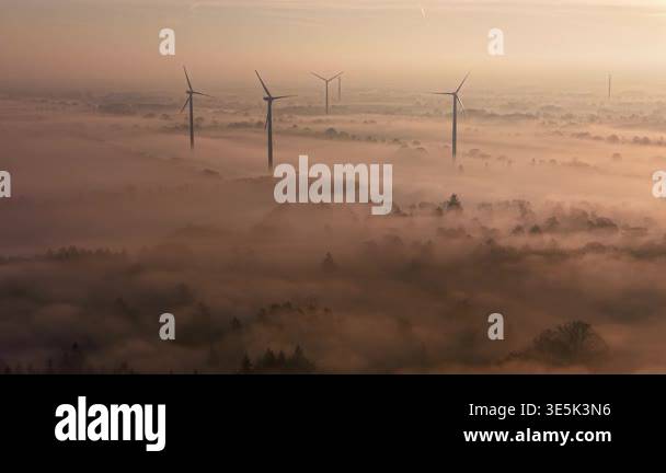 Cinematic aerial view of wind turbines rising above thick morning fog ...