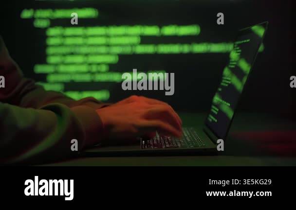 Close-up of anonymous hacker hands typing on laptop with glowing green ...
