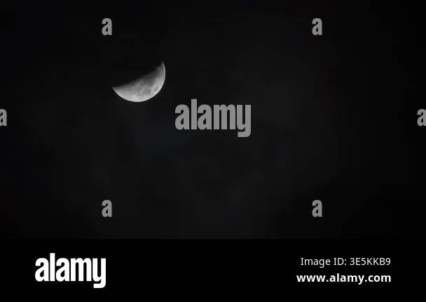 Crescent moon partially covered by thin clouds in a dark night sky ...