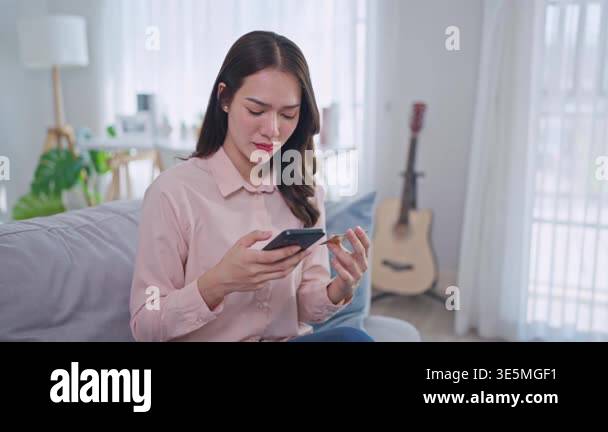 Asian woman using mobile phone shopping online in living room at home ...