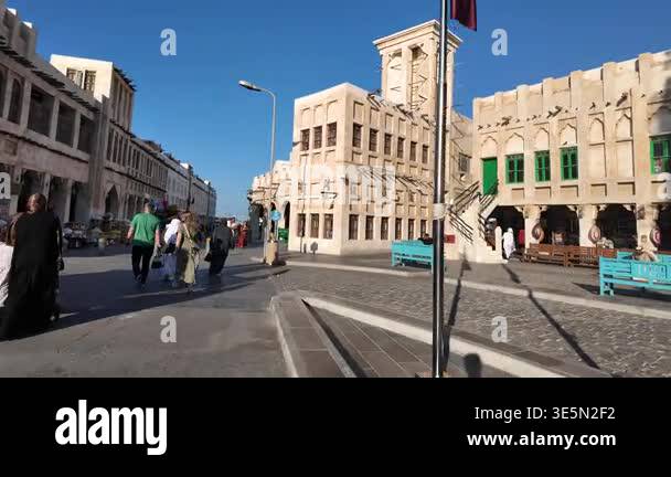 People walk along a street in Doha with old buildings nearby Stock ...