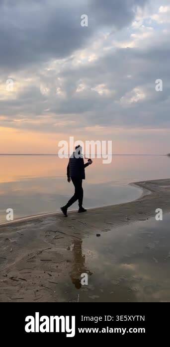 Rear view of a man walking on a deserted beach under a dramatic cloudy ...