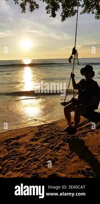A person wearing a black hat and shirt sits on a simple wooden swing ...