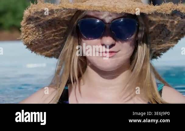 Young woman relaxing in swimming pool wearing sunglasses and straw hat ...