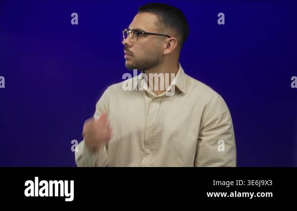 Man wearing glasses with hand on chin for thinking in a blue studio ...