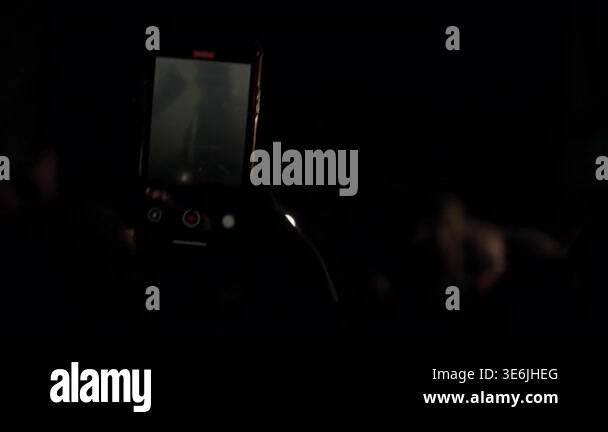 A person films a live concert or event with a smartphone in a dark ...