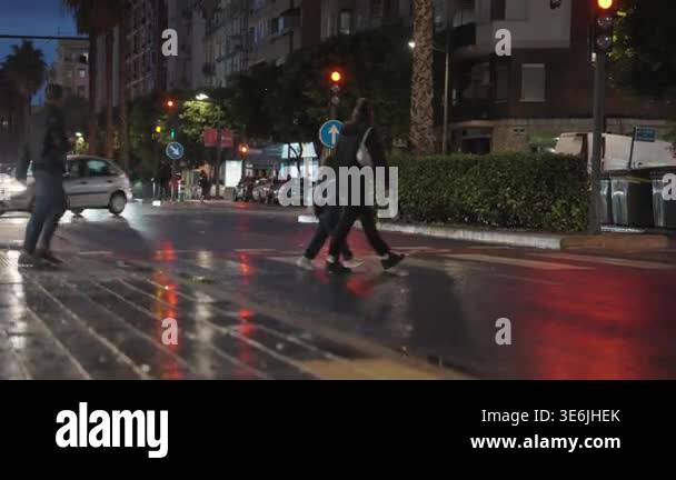 VALENCIA, SPAIN - JANUARY 23, 2026: Pedestrians cross a wet city street ...