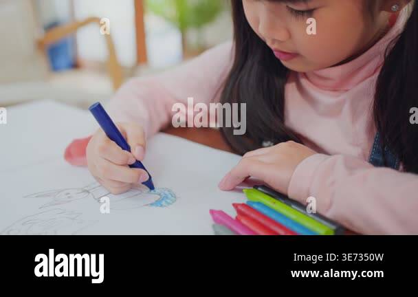 Girl drawing with blue marker on paper at a table filled with colorful ...