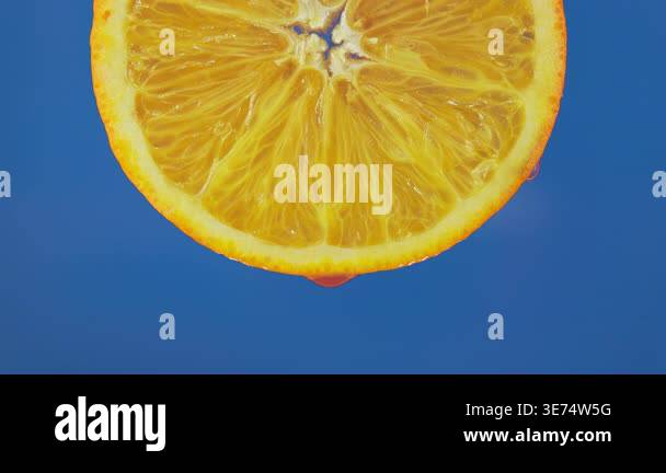 A cross-cut orange slice is squeezing its juice in a macro shot with a ...