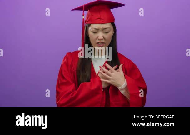 Woman wearing red graduation gown stands against a purple background ...