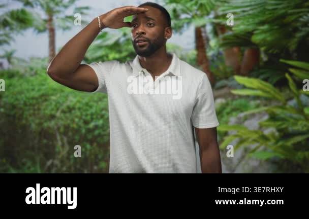 Man in white polo shirt with hand to forehead looking toward treeline ...