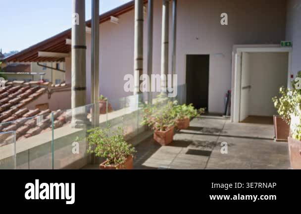 Terrace with glass railing, potted plants and tiled roof, defocused ...