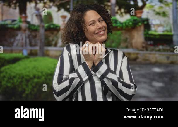Hispanic woman smiling forms heart gesture with hands in forest under ...