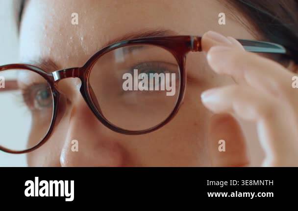 A woman with light skin is adjusting her glasses indoors. She is ...
