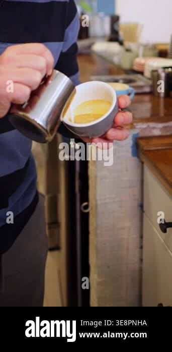 Professional barista pouring steamed milk from a steel pitcher into a ...