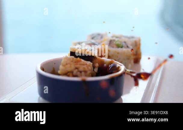 A sushi piece falls into a deep blue bowl with soy sauce, splashing ...