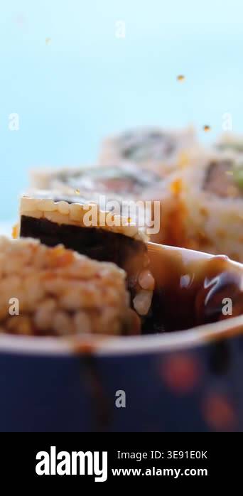 A sushi piece falls into a deep blue bowl with soy sauce, splashing ...