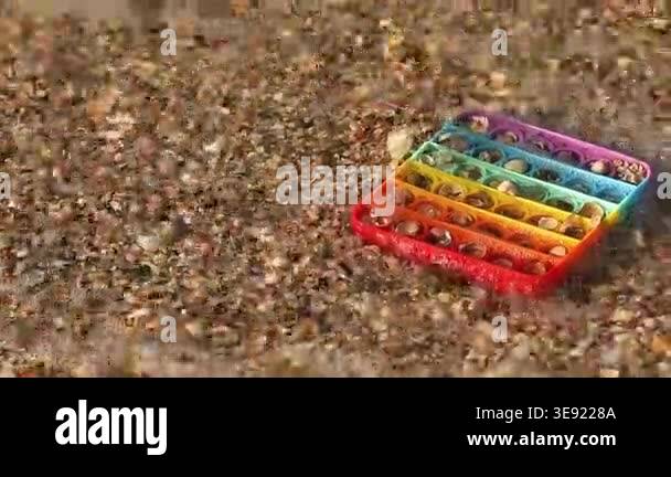 Colorful silicone pop it toy on shore with foamy water approaching ...