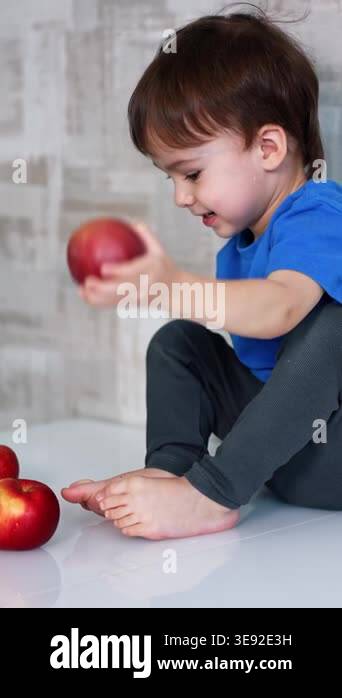 Caucasian toddler in blue t-shirt and grey pants sits playing with red ...
