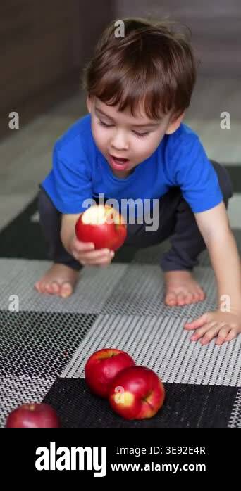 Lovely toddler squatted on the floor near few apples on the carpet. Kid ...