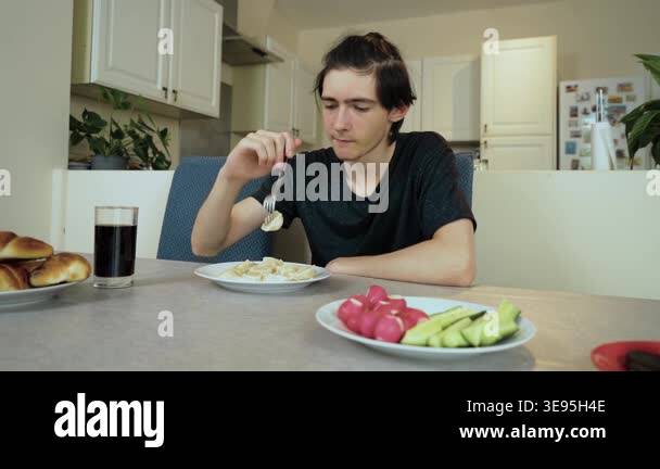 Meal in kitchen with young man eating dumplings and looking calm ...