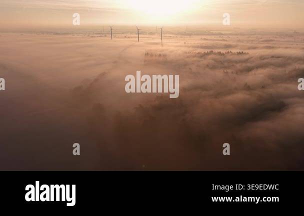 Cinematic aerial view of wind turbines rising above thick morning fog ...