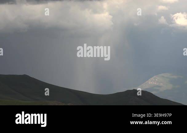Natural real rain falling from clouds onto treeless hills and mountains ...